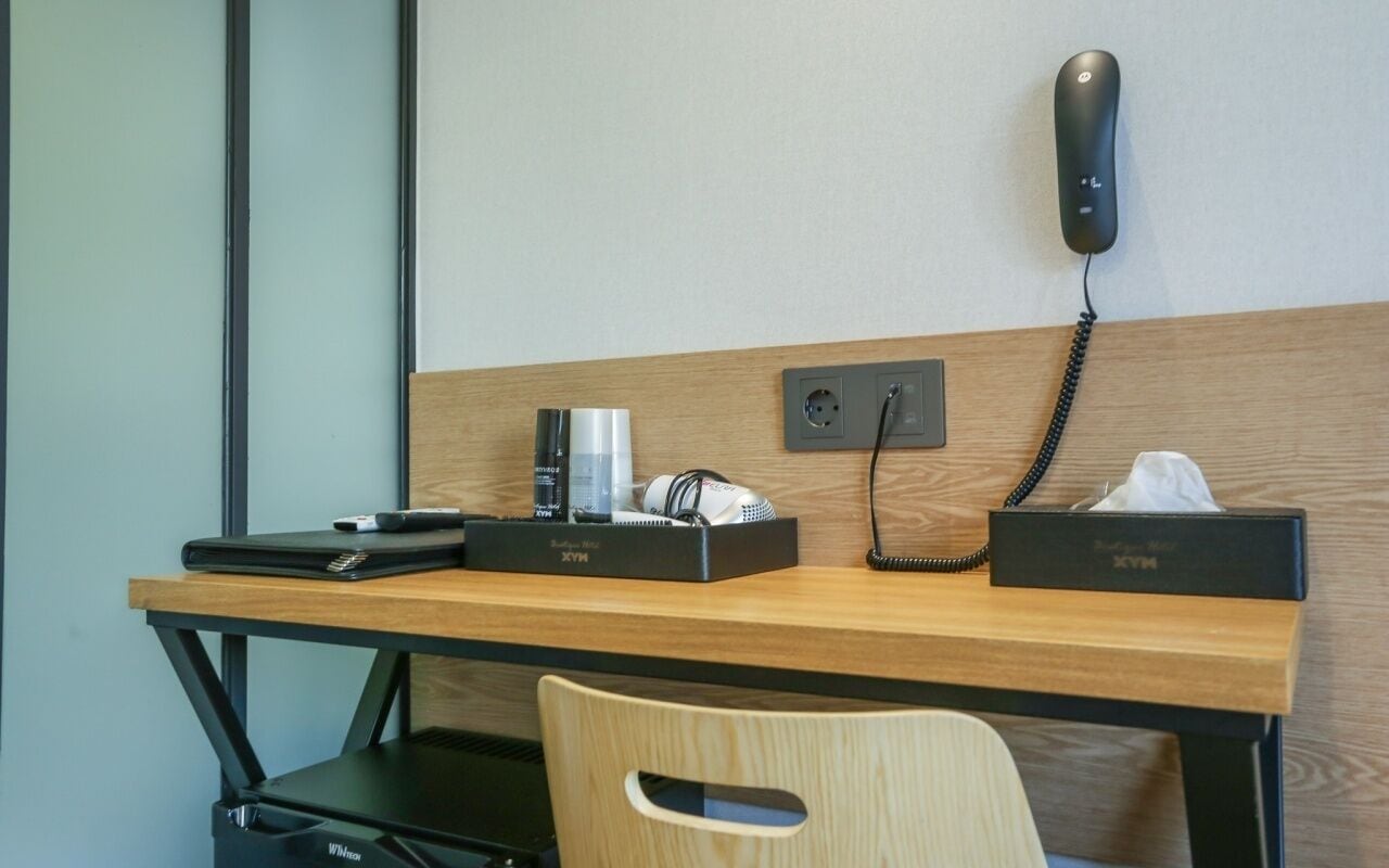 Mesa de quarto de hotel com um laptop, um estojo de lenços de papel, um telefone e uma tomada.