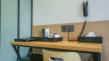 Mesa de quarto de hotel com um laptop, um estojo de lenços de papel, um telefone e uma tomada.