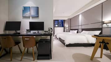Quarto de hotel moderno com escrivaninha, dois monitores, uma impressora, duas cadeiras, cama com lençóis brancos e uma janela grande com cortinas.