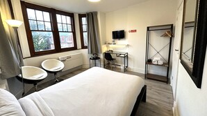 Quarto de hotel com cama, escrivaninha, cadeira, televisão e guarda-roupa.