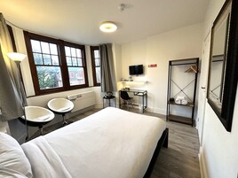 Quarto de hotel com cama, escrivaninha, cadeira, televisão e guarda-roupa.