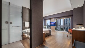 Quarto de hotel moderno com uma cama grande, uma escrivaninha e vista para a paisagem urbana através de amplas janelas.
