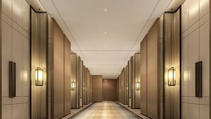Um corredor moderno de hotel, com layout longo e reto, iluminação embutida e carpete estampado.