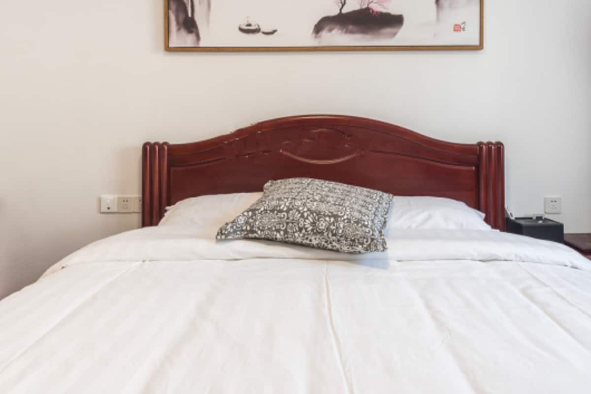 Cama com cabeceira de madeira, roupa de cama branca e almofada decorativa.