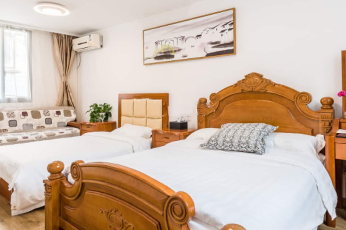 Quarto com duas camas de solteiro, cabeceira de madeira, mesa de cabeceira, janela com cortinas, ar condicionado e um quadro na parede.