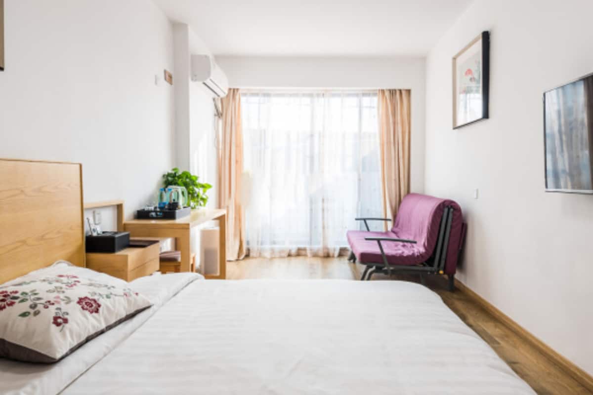 Quarto com cama, escrivaninha, cadeira e janela com cortinas.