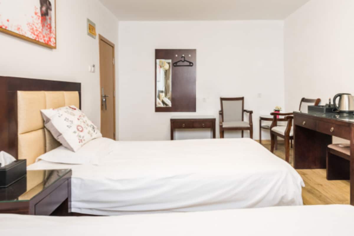 Quarto de hotel com cama, escrivaninha, cadeira, espelho e quadro na parede.