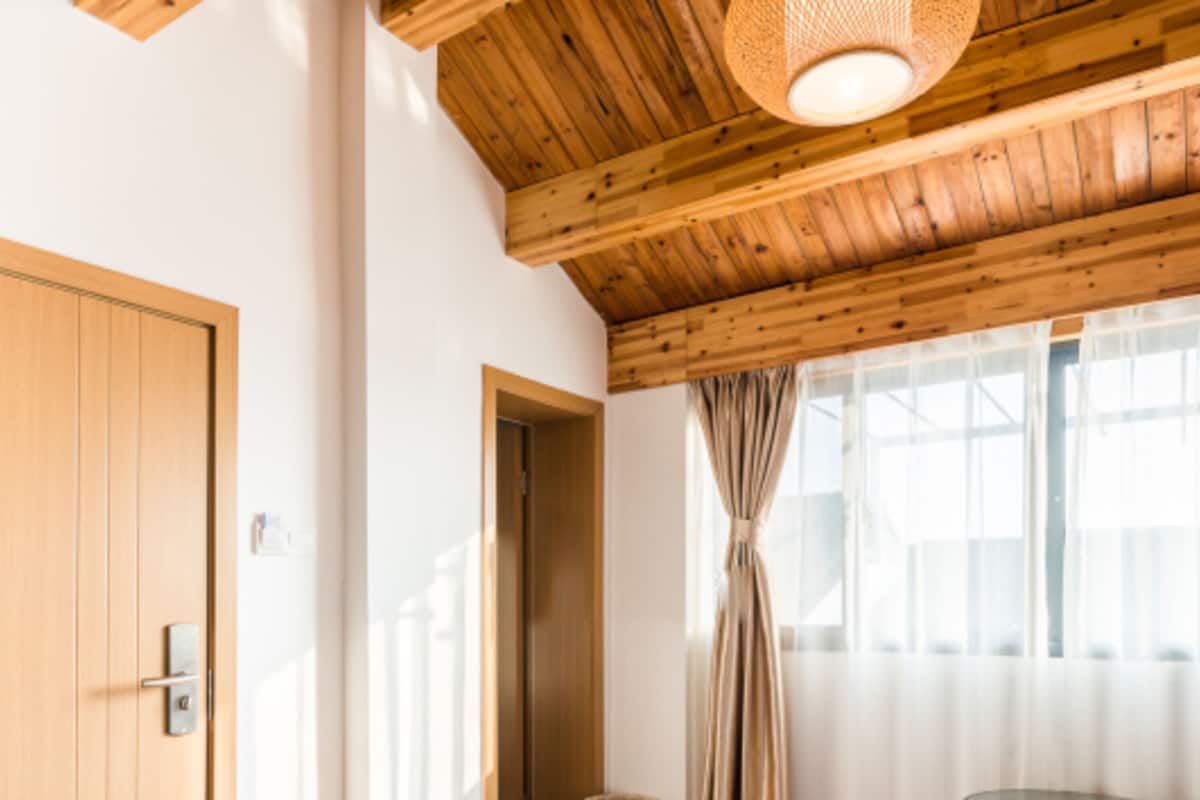 Quarto com teto de madeira, uma cama, janela com cortinas e uma pequena mesa.