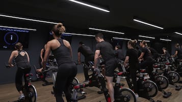 Um grupo de pessoas se exercitando em bicicletas ergométricas em uma academia com espelhos nas paredes.