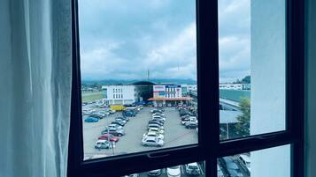 Vista da janela sobre um estacionamento com vários carros e um edifício com a placa 'Panasonic'.