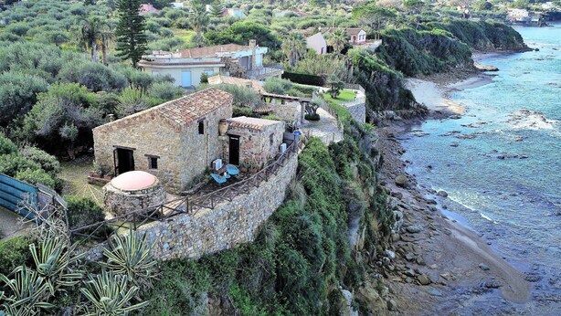 Um edifício de pedra à beira-mar com um pequeno alpendre, com vista para a costa rochosa.