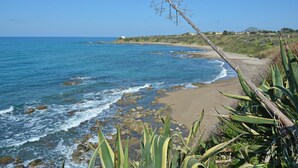 Paisagem costeira com praia de areia, falésias rochosas e vegetação.