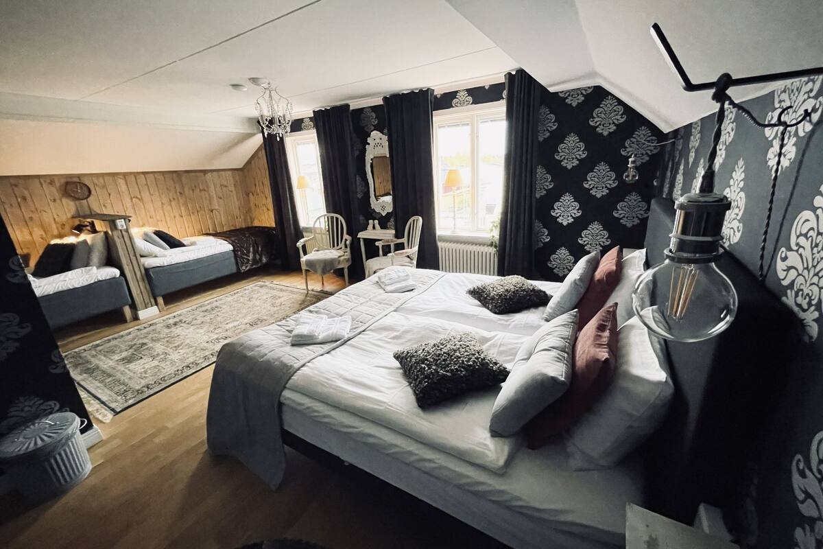 Quarto com uma cama grande, escrivaninha, cadeira e janela com cortinas.