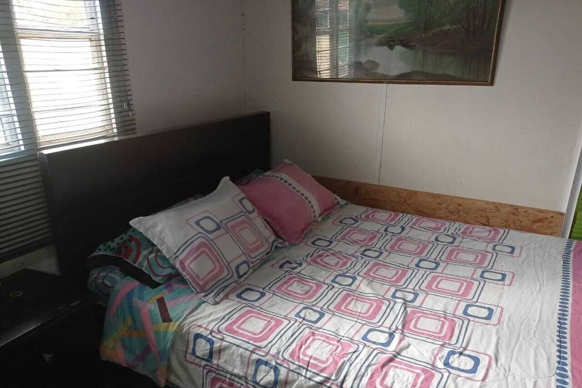 Uma cama com colcha estampada, cabeceira e janela com persianas.