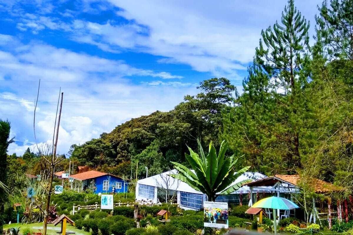 Uma vila rural com casas tradicionais, vegetação exuberante e um céu claro.