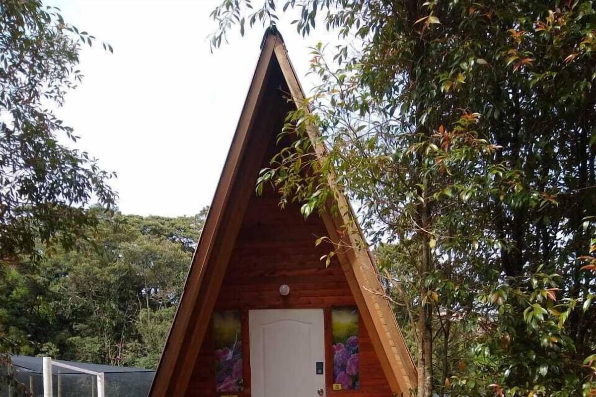 Uma cabana de madeira com telhado triangular, uma porta branca e duas cadeiras de plástico brancas na varanda.