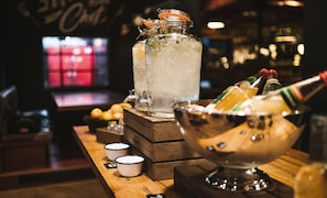 Uma área de bar com um grande recipiente de vidro cheio de gelo, uma tigela de metal com garrafas e pequenas tigelas sobre uma superfície de madeira.