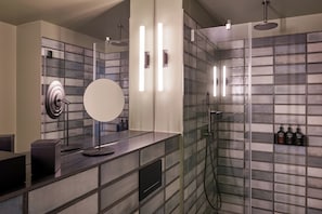 Uma casa de banho moderna com cabine de chuveiro em vidro, um espelho redondo e bancada com produtos de higiene pessoal.