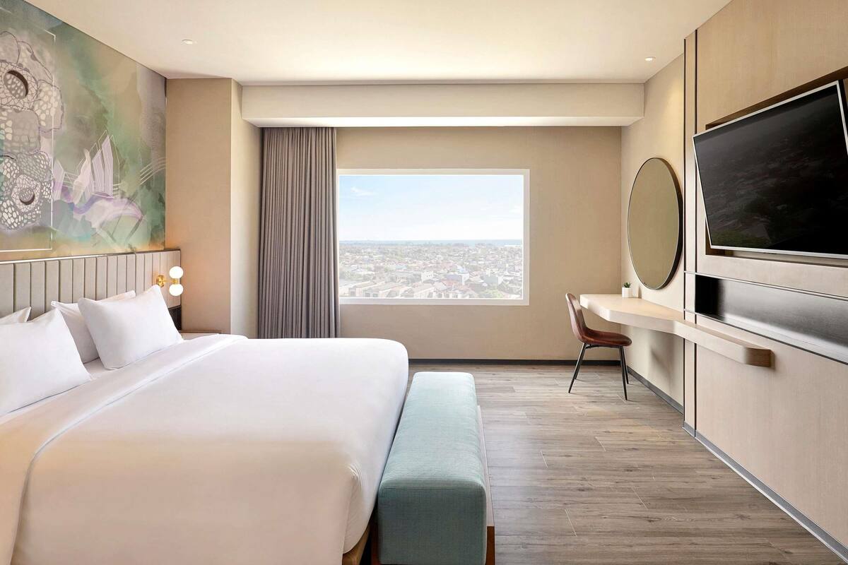 Quarto de hotel com uma cama grande, uma escrivaninha, uma TV e uma janela com vista para a cidade.