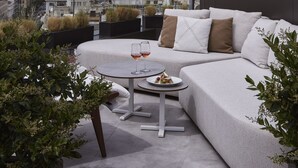 Terraço no telhado com um sofá moderno, uma mesa pequena com copos e uma bandeira.