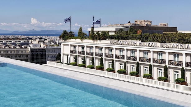 Um hotel com piscina, bandeiras e vista para um edifício histórico ao fundo.