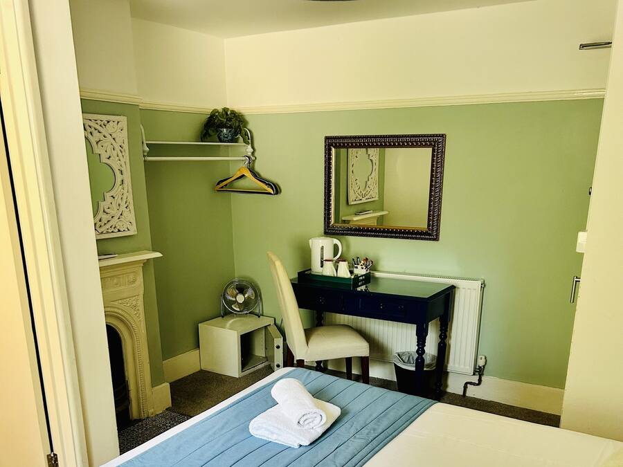 Quarto de hotel com cama, escrivaninha, cadeira, espelho e radiador.