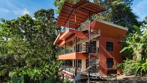 Um edifício de vários andares com fachada vermelha, rodeado por vegetação exuberante.