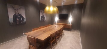 Uma sala de conferências com uma longa mesa de madeira, várias cadeiras, um grande lustre e duas quadros nas paredes.