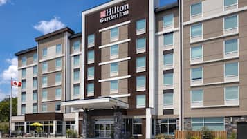 Um Hilton Garden Inn de vários andares com design arquitetônico moderno, apresentando uma entrada destacada com toldo e um mastro com a bandeira canadense.