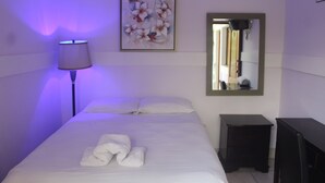 Quarto de hotel com cama, abajur, espelho e um quadro na parede.