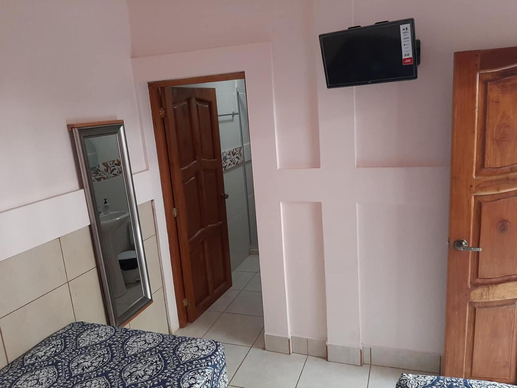 Quarto com uma cama, televisão fixada na parede, porta de madeira e espelho na parede.