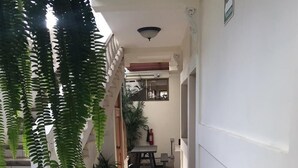 Um corredor com uma escada à esquerda, uma área de refeições com mesa e cadeiras ao centro, e uma parede branca à direita.