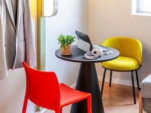 Um quarto com uma mesa redonda, um laptop, auscultadores, uma planta em vaso, uma cadeira vermelha e uma cadeira amarela.