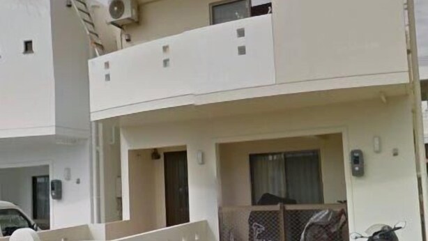 Um edifício residencial de dois andares com varanda, uma motocicleta estacionada em frente e portão de acesso.