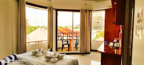 Quarto de hotel com uma cama, uma mesa com cadeiras, um armário vermelho e vista para edifícios através de amplas janelas.