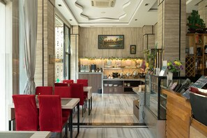 Restaurante moderno com cadeiras vermelhas, piso de mármore e área de cozinha com plantas e utensílios.