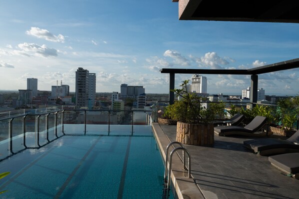 Uma piscina infinita no terraço com vista para a cidade, espreguiçadeiras e um pérgola.