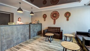 Uma área de recepção com balcão de check-in, um sofá, duas mesas redondas e arte decorativa na parede.