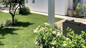 Uma casa moderna com fachada branca, um espaço de varanda coberto e um jardim bem cuidado com gramado e arbustos de hortênsia.
