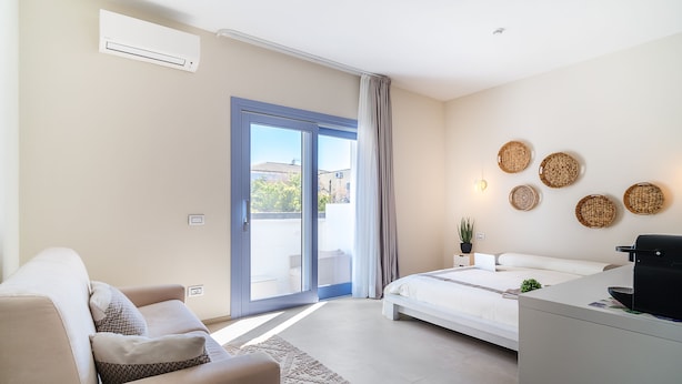 Quarto moderno com cama, sofá, máquina de café e vista por uma porta deslizante.
