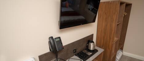 Quarto de hotel com televisão de tela plana na parede, escrivaninha com telefone, cafeteira e secador de cabelo.