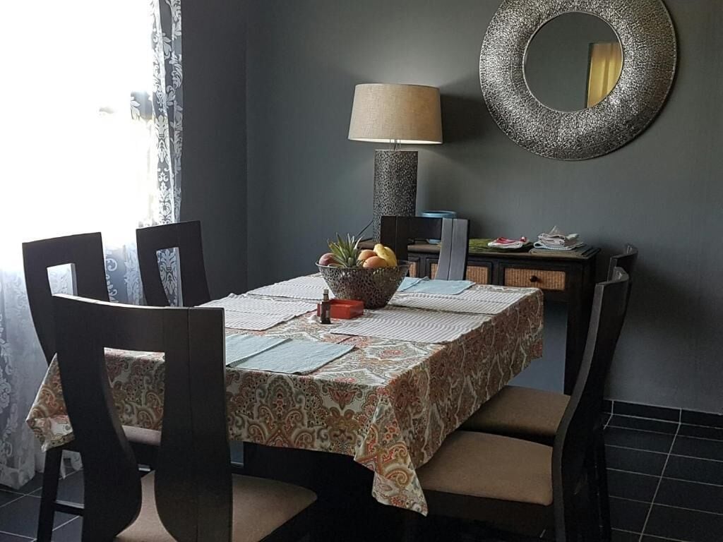 Uma sala de jantar com mesa posta para dois, uma cesta de frutas e um abajur.