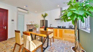 Uma sala de jantar com mesa e cadeiras de madeira, uma cozinha com armários de madeira e uma planta em vaso.