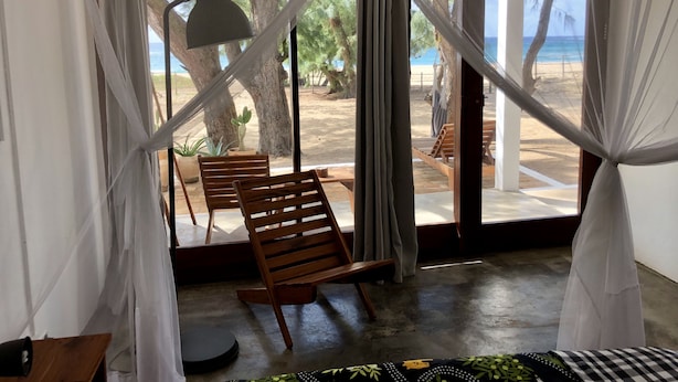 Quarto com vista para a praia, com rede, cadeiras de madeira e uma mesa.