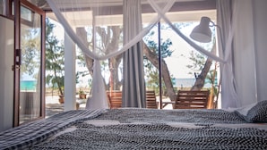 Quarto com cama, cortinas e vista para a praia.