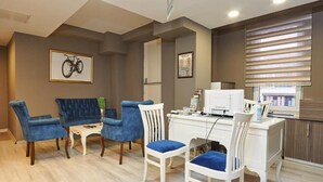 Quarto com área de jantar, uma escrivaninha branca com computador e uma janela com persianas.