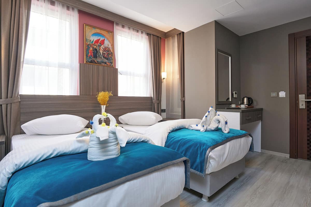 Quarto de hotel com duas camas, uma escrivaninha, um espelho e um quadro na parede.