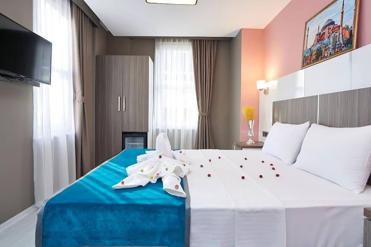Quarto de hotel com cama, televisão, guarda-roupa e um quadro na parede.