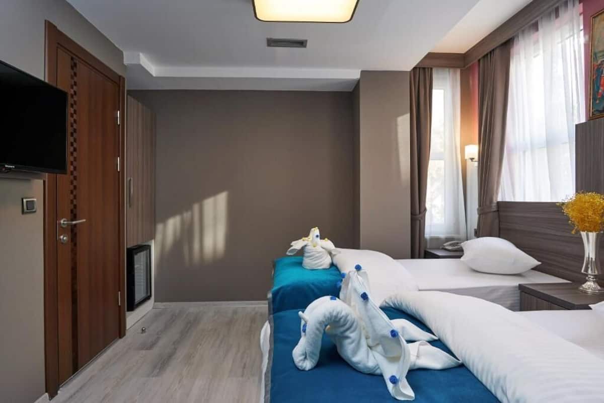 Quarto de hotel com duas camas, televisão, guarda-roupa e janela com cortinas.