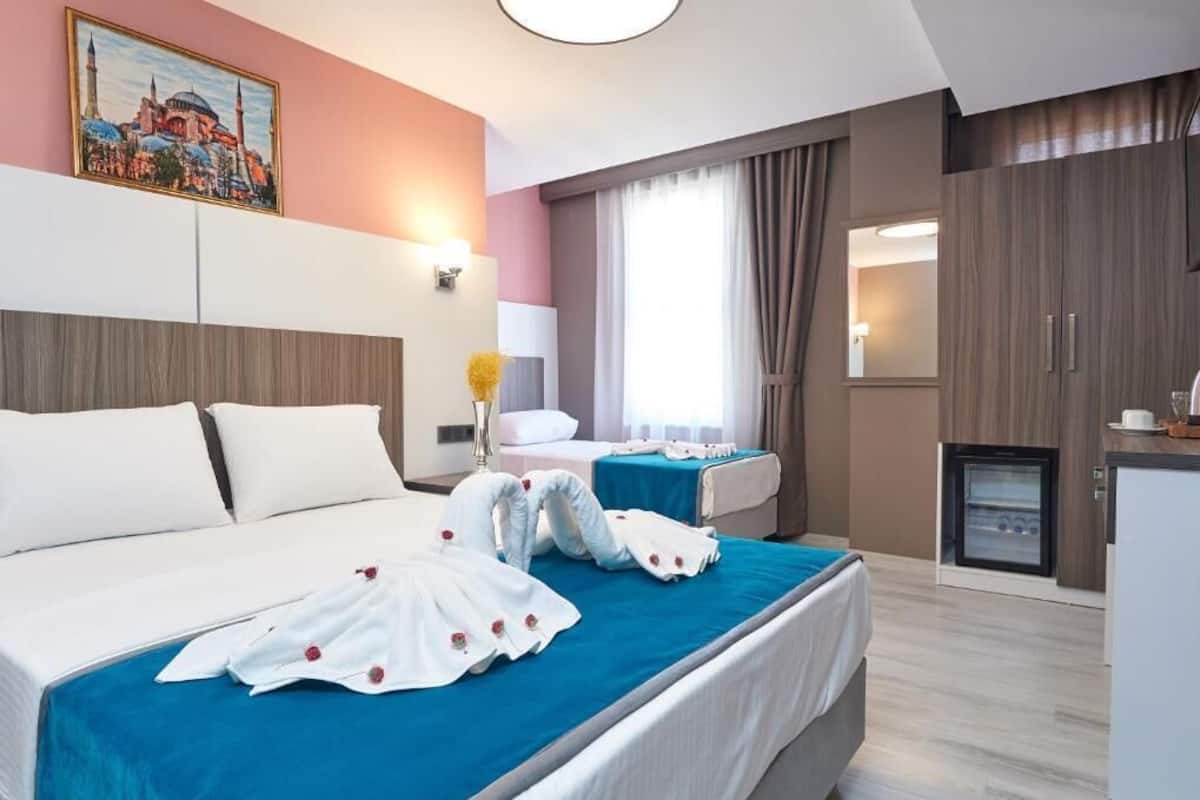Quarto de hotel com duas camas, um minibar, uma televisão pequena e um quadro na parede.